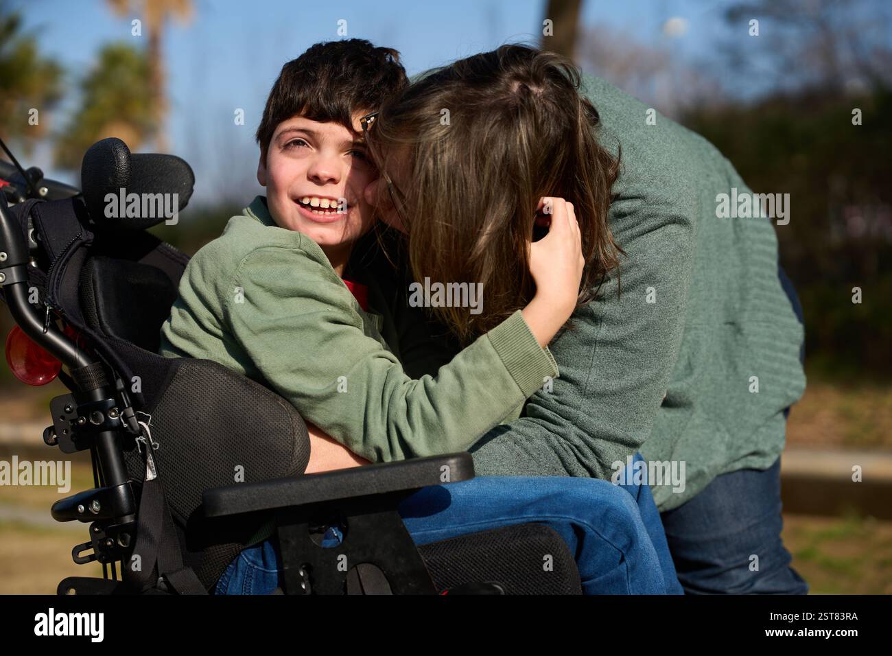 Boy with disability hugging his mother in a wheelchair in the park ...