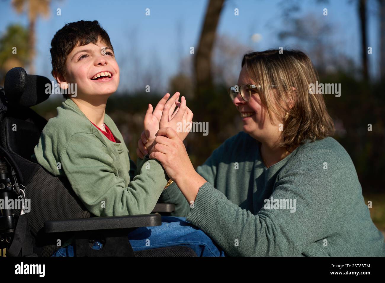 Therapist assisting child with disability in wheelchair outdoors ...