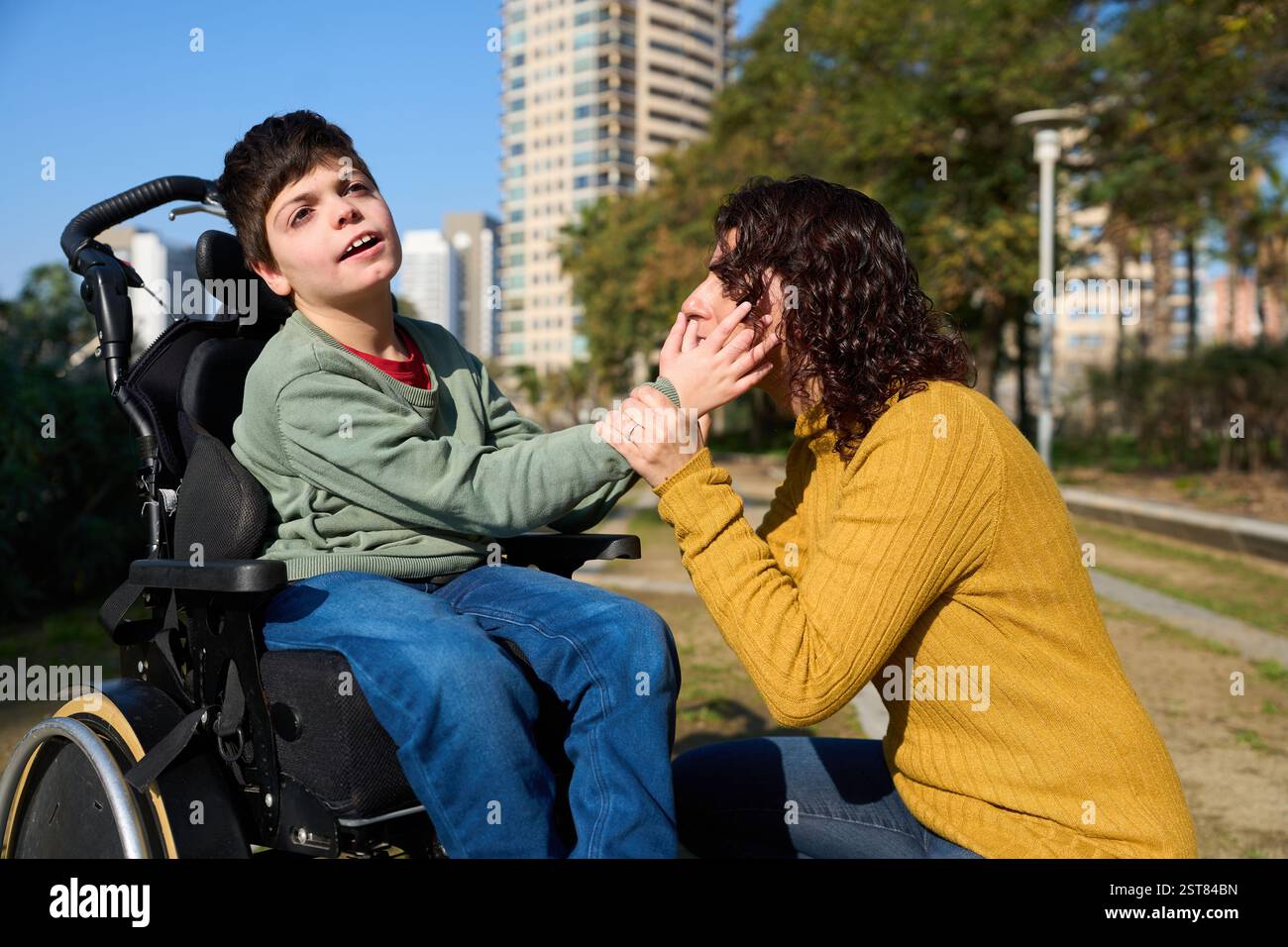 Boy with disability touching mother's face while sitting in wheelchair ...