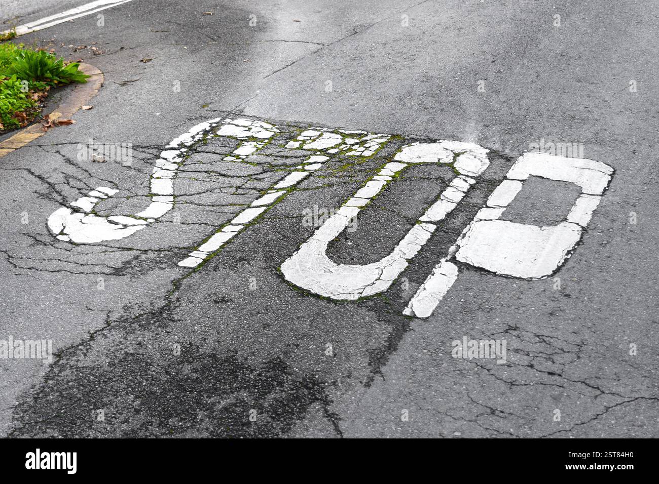 Faded white STOP sign painted on cracked asphalt road with wear and ...