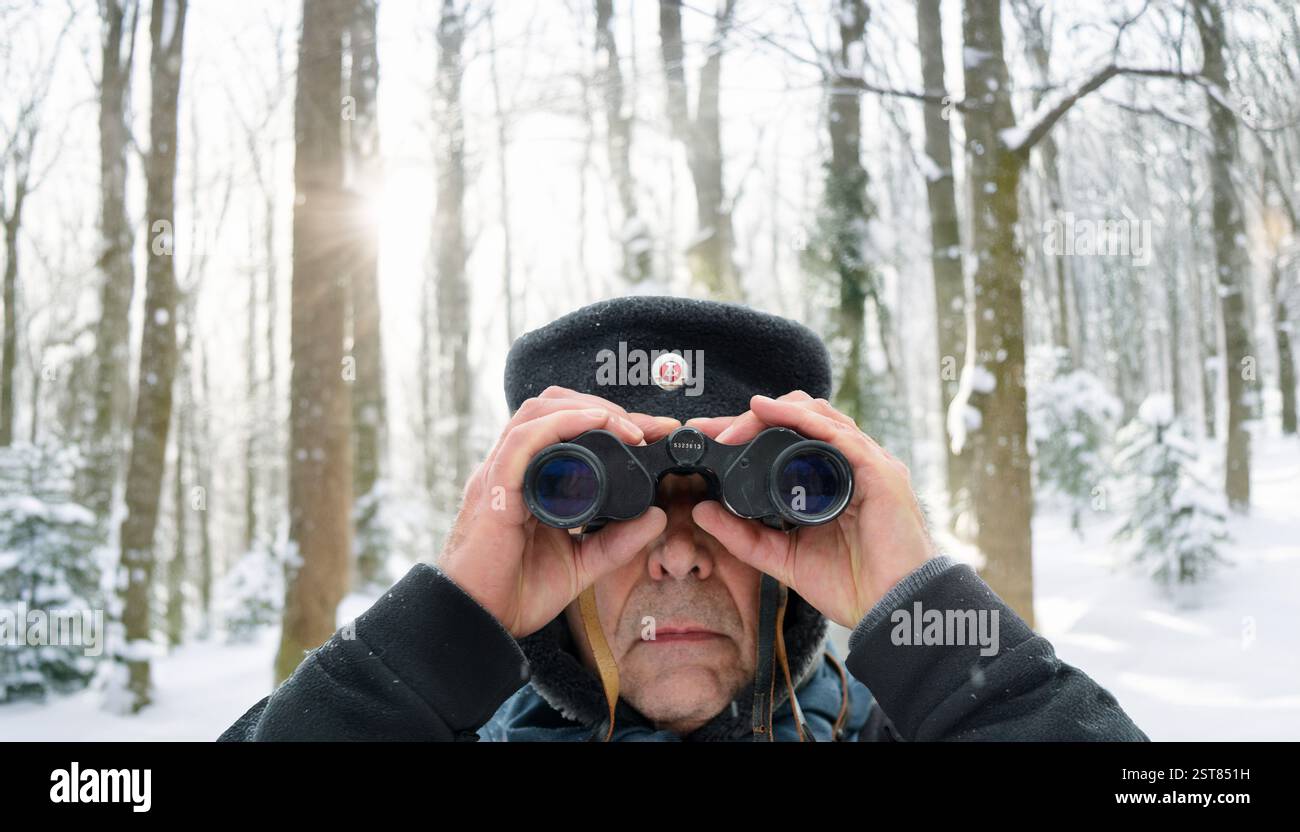 Man looking through binoculars wearing old East German border guard hat ...