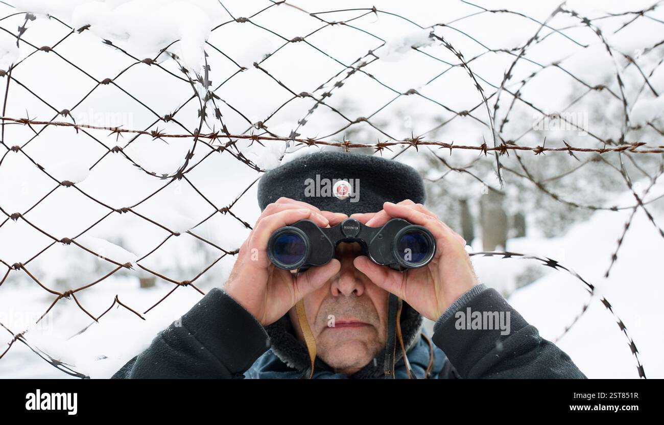 Man looking through binoculars wearing old East German border guard hat ...