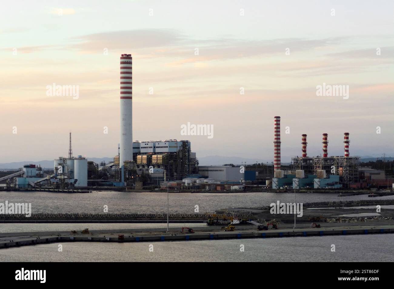 A power plant with distinctive striped smokestacks near the coastline ...