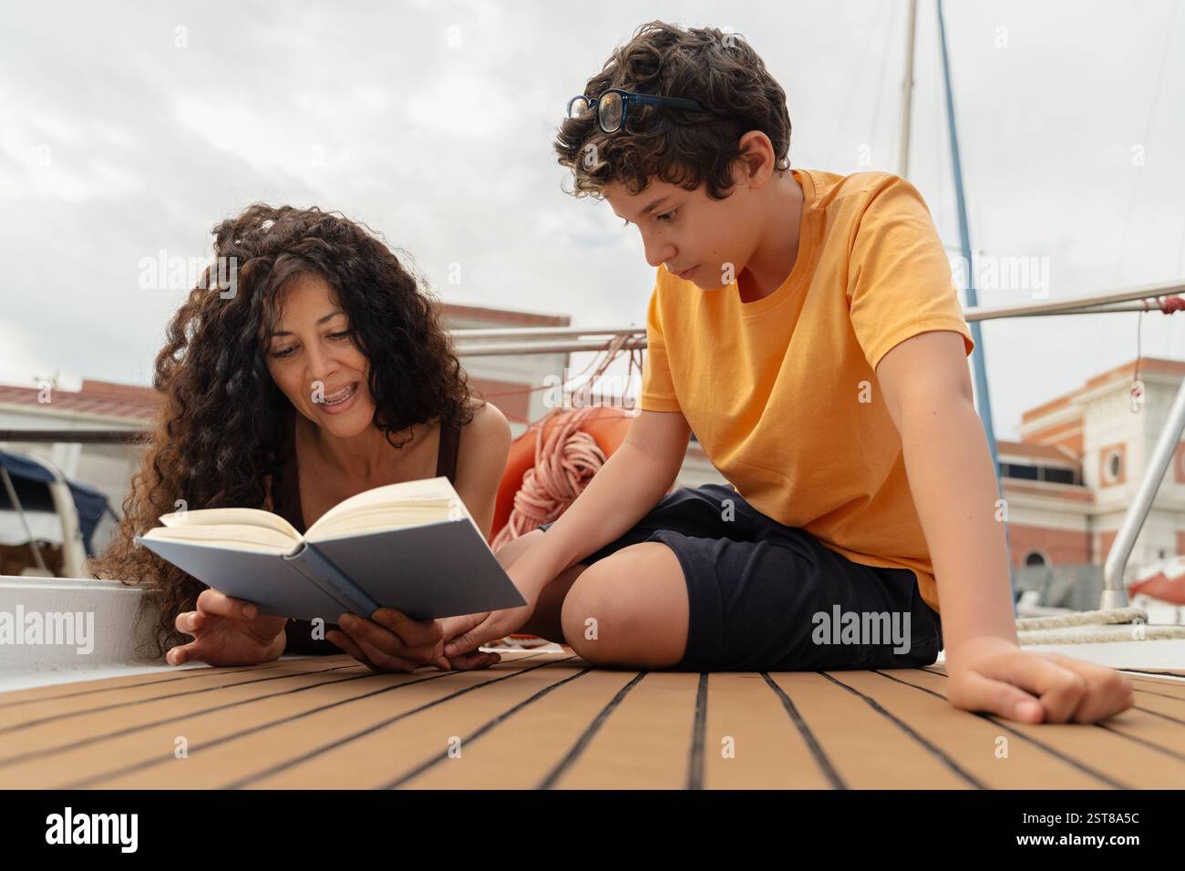 A mother and her son reading a book together on a sailing boat ...