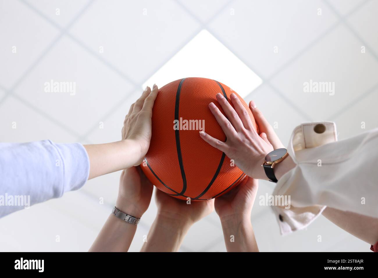 Unity concept. People holding basketball ball together indoors, low ...