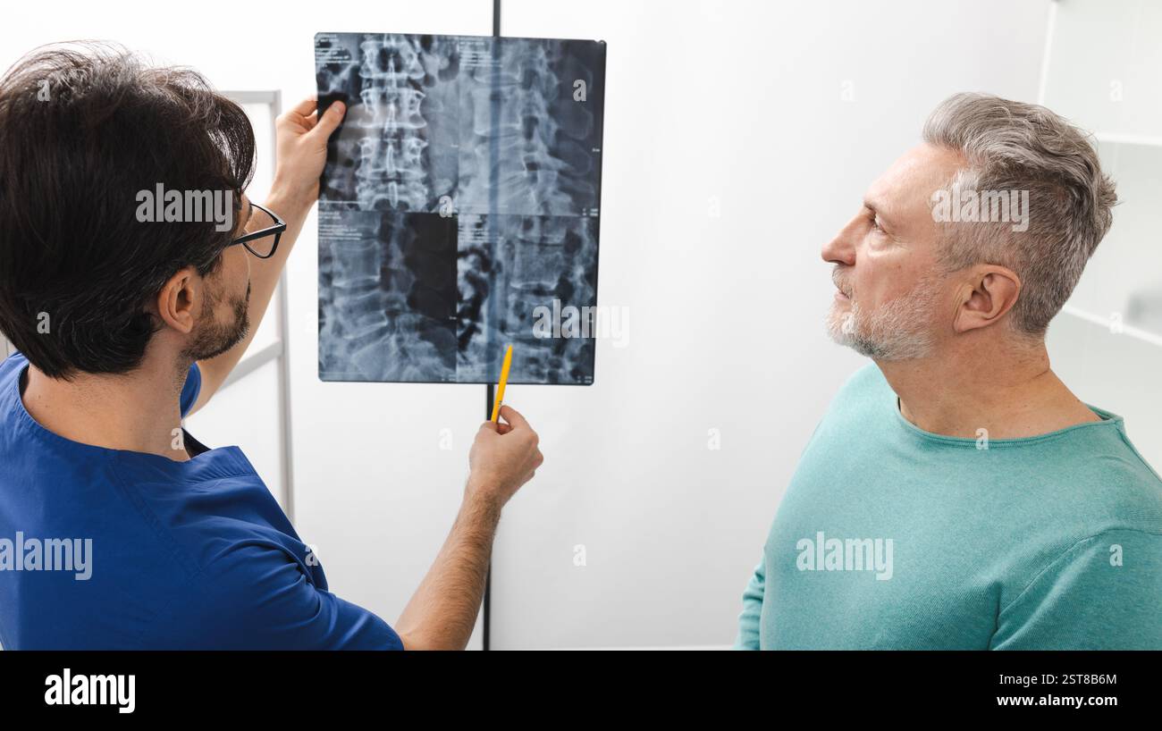 Manual therapist viewing X-ray of backbone with his mature male patient ...