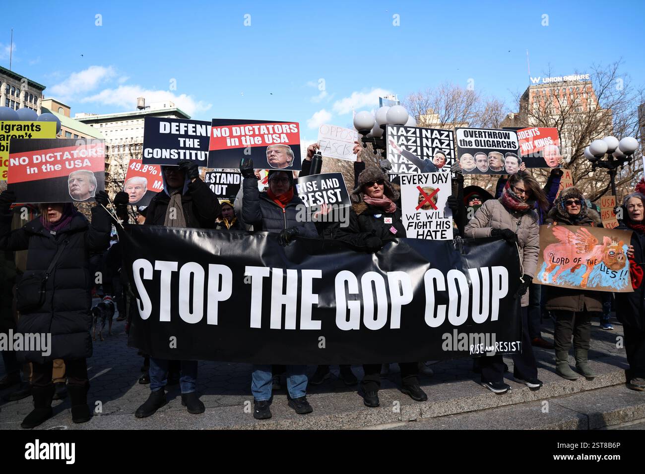People hold up a banner and placards opposed to the policies of ...