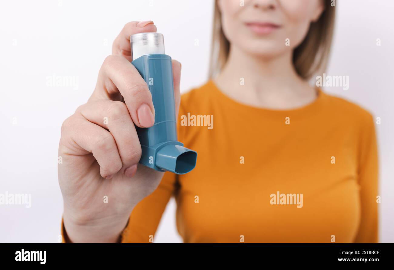 Woman holding portable asthma inhaler while standing on white ...