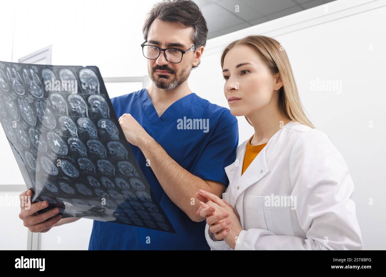 Two healthcare specialists closely examine brain MRI scans in a medical ...