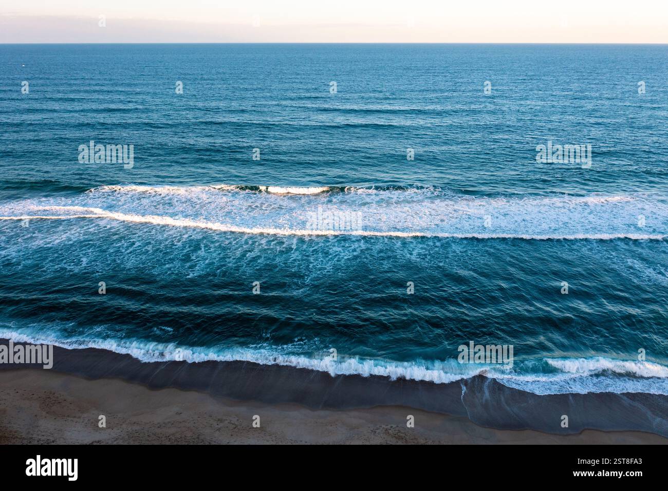 Aerial view top down of waves breaking on the beach in Kill Devil Hills North Carolina at sunset ...