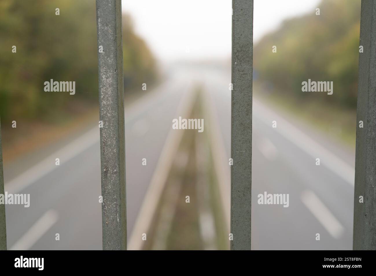 Photo of an empty highway through the fence of the bridge above it ...
