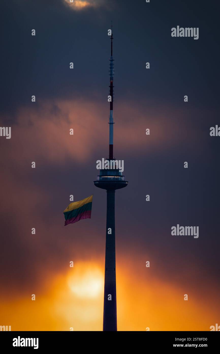 The Vilnius TV Tower standing tall against a dramatic sunset sky, with the Lithuanian flag ...