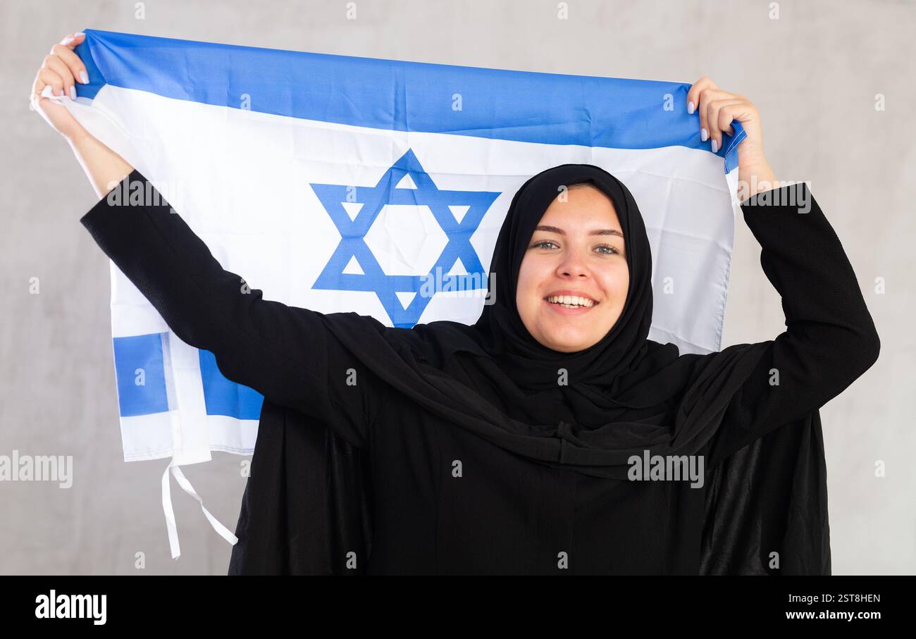 Balanced smiling Muslim woman in traditional black hijab holds flag of ...