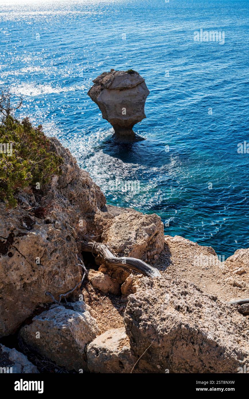 A uniquely shaped rock formation stands in the crystal-clear blue ...