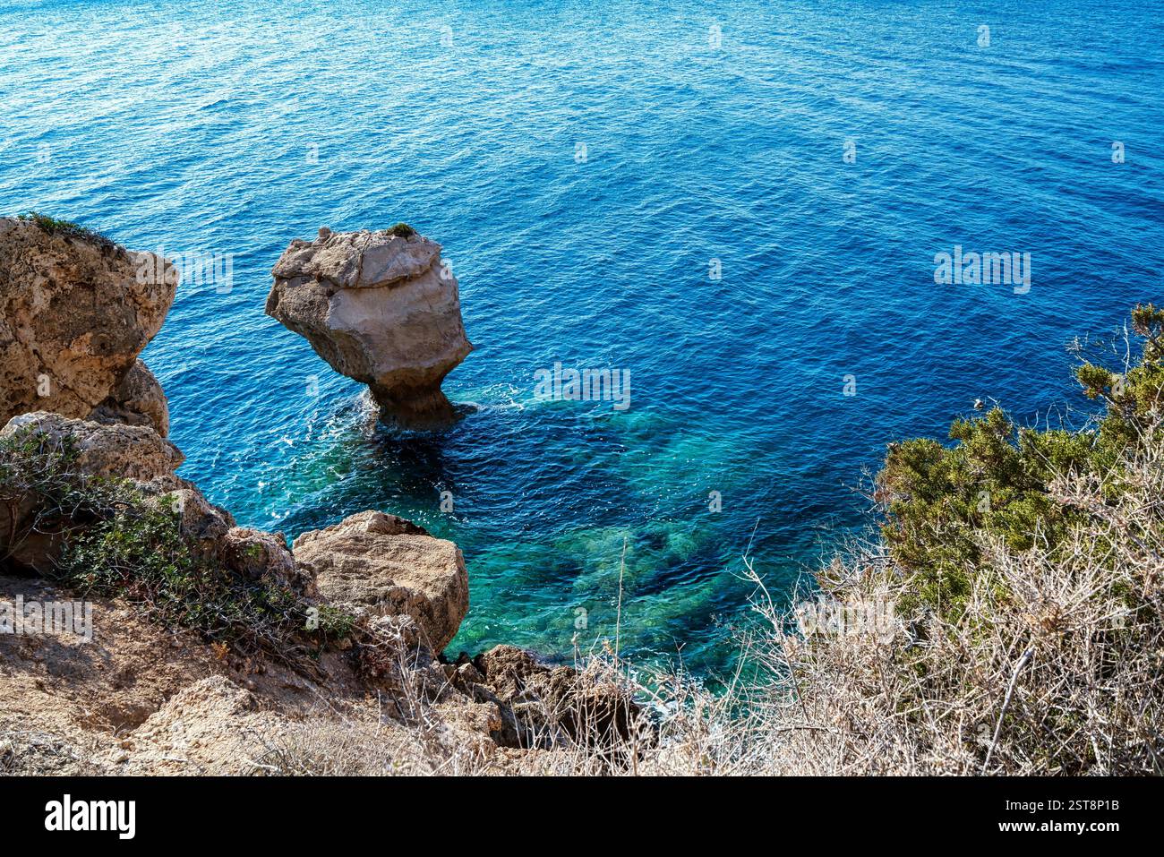 A uniquely shaped rock formation stands in the crystal-clear blue ...