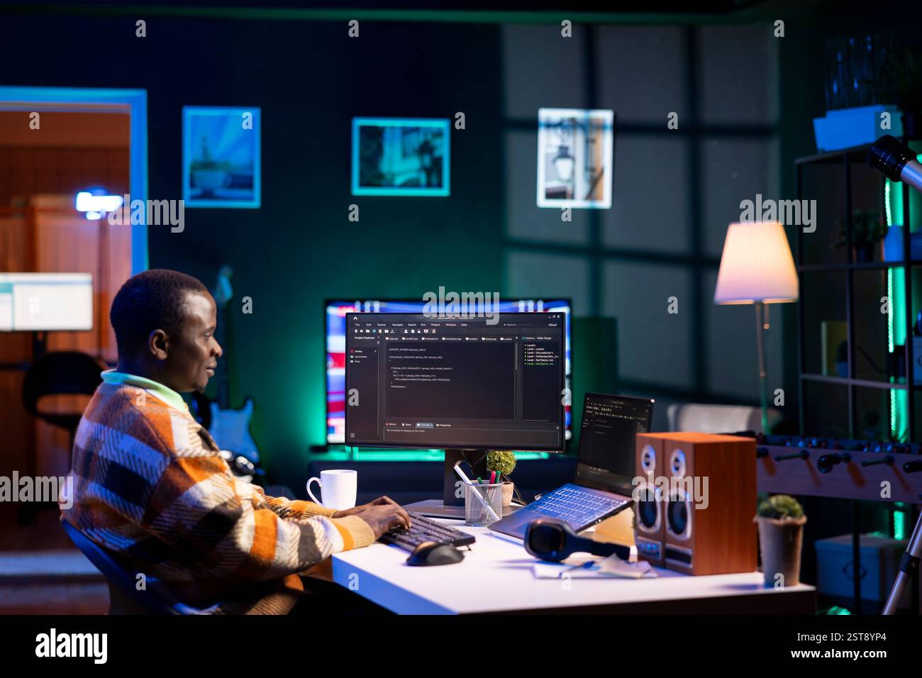 Programmer in home office concentrating on finding bugs while he codes on his computer. African ...
