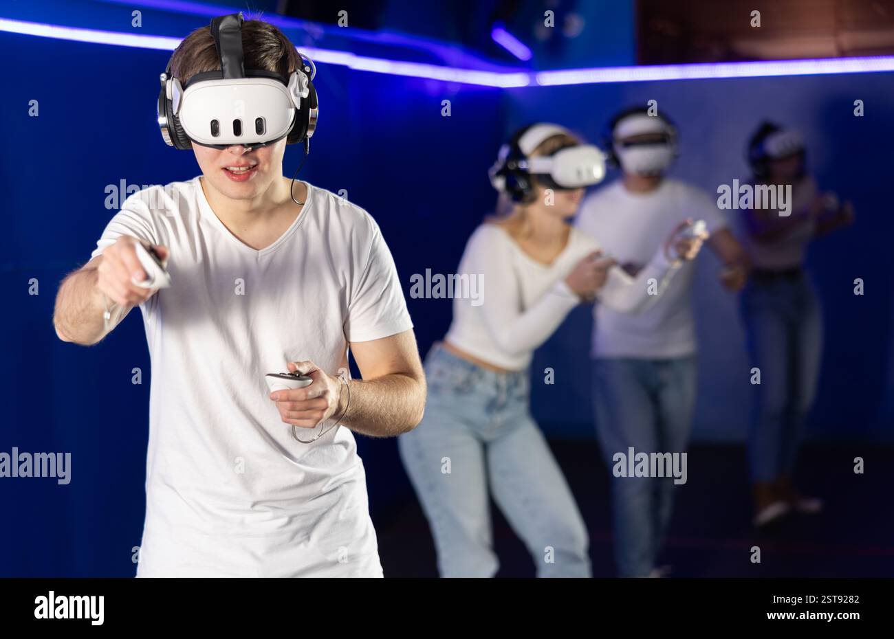 In darkened hall of gaming club, guy in VR helmet takes part in group ...