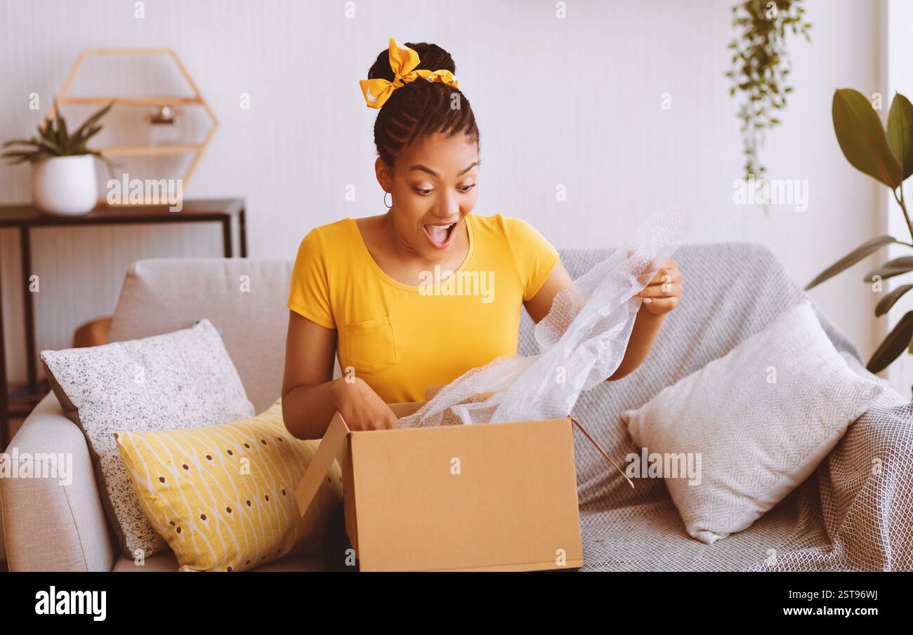 Excited black woman unpacking box after online shopping Stock Photo - Alamy