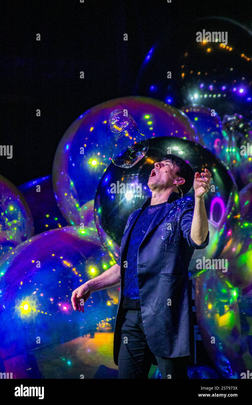 Using a bubble pipe, a young Asian American man creates huge bubbles at ...