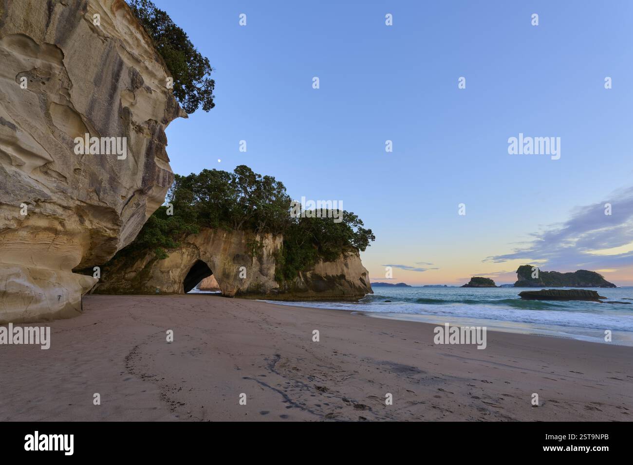 View of a cave on the beach, the sea and a softly coloured sunrise ...