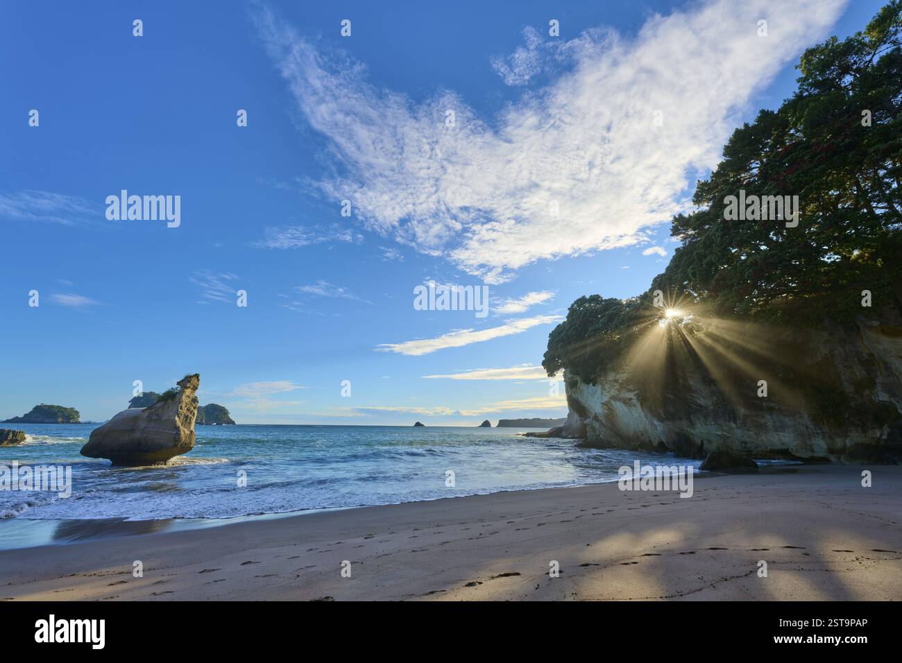 Landscape with sandy beach and bright sun behind rocks by the sea ...