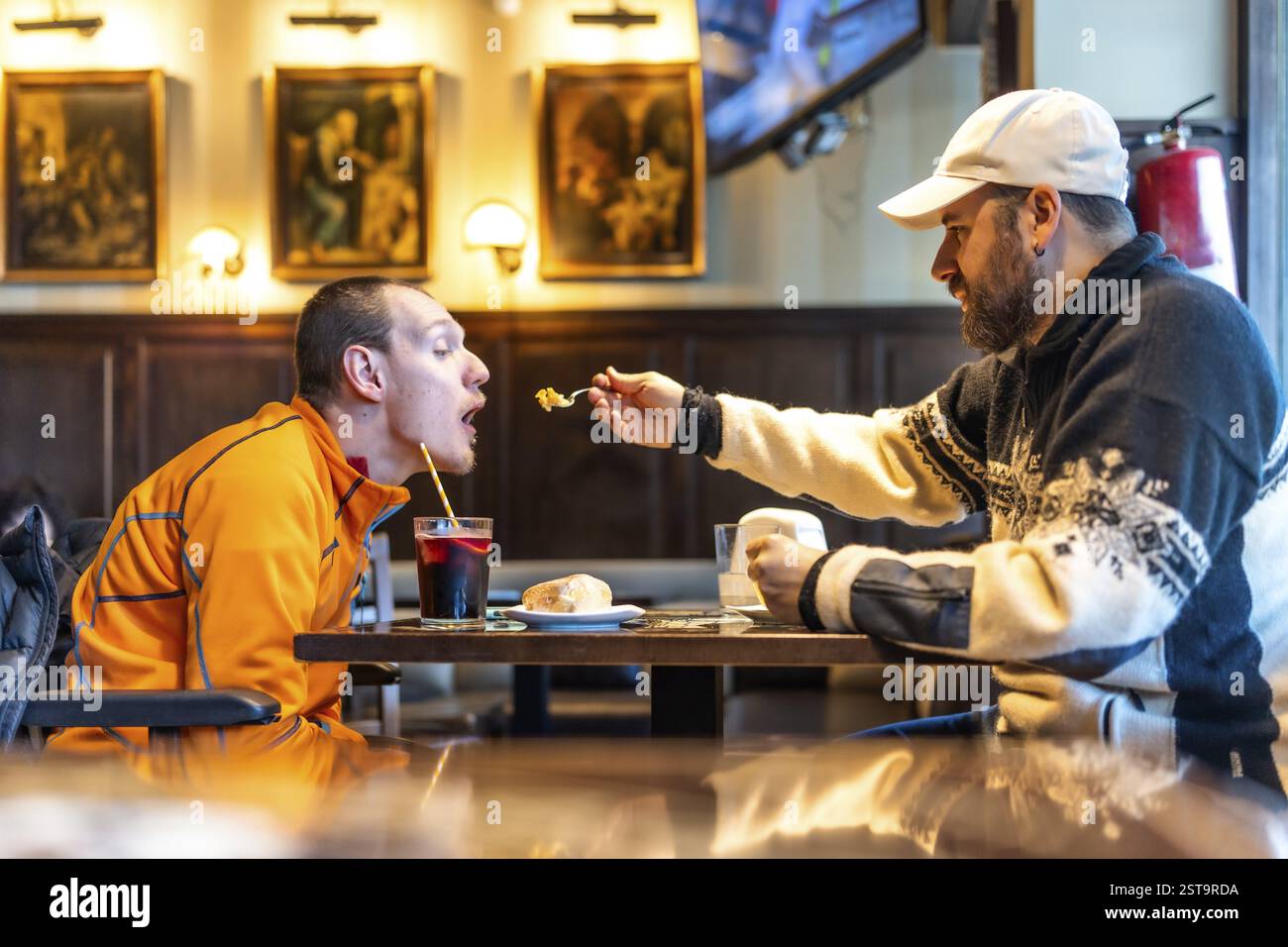 Man feeding his disabled friend in a restaurant, showcasing genuine ...
