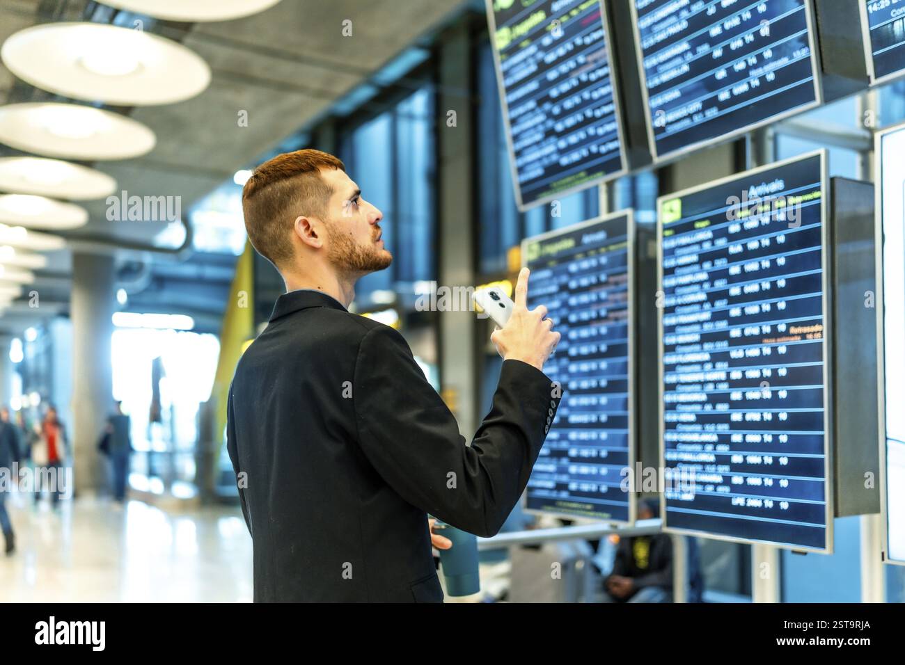 Businessman holding smartphone and pointing at timetable display ...