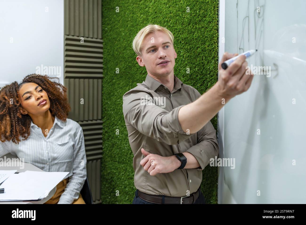 Manager drawing on a whiteboard while explaining strategy to a coworker ...