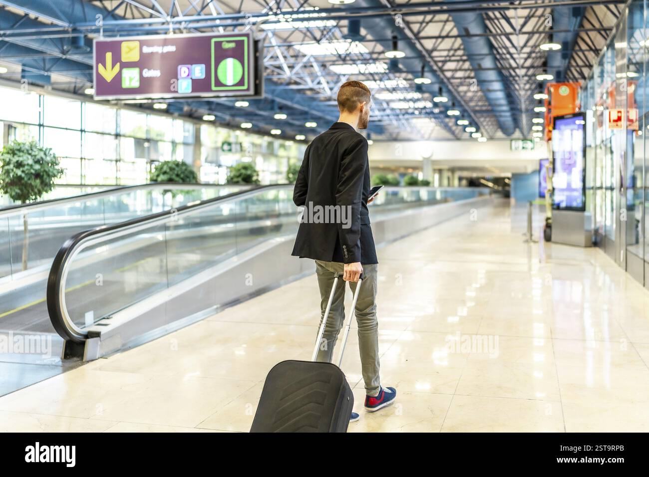 Businessman pulling trolley and using smartphone while walking in ...