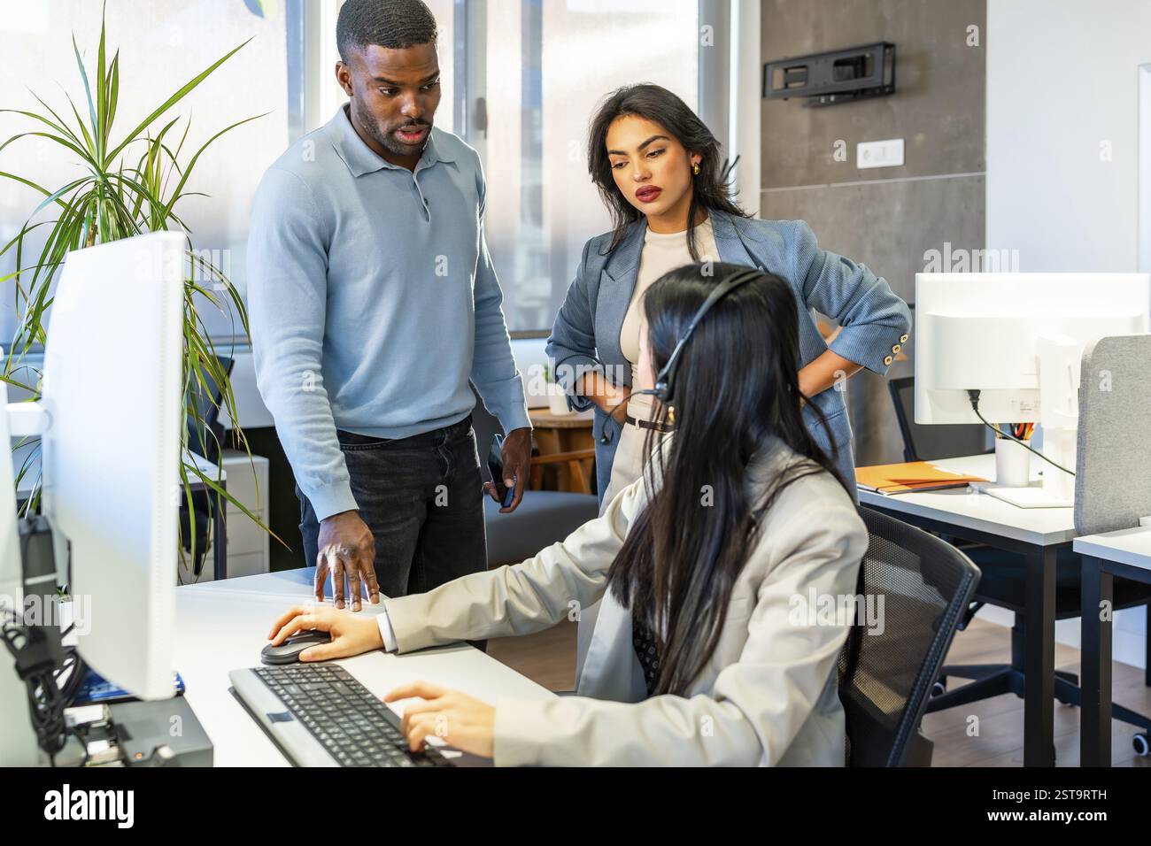 Office workers assisting a colleague using a computer and wearing a ...