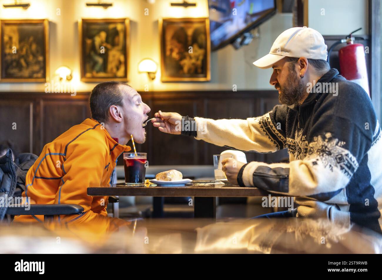 Man feeds his disabled friend in a restaurant, demonstrating care ...