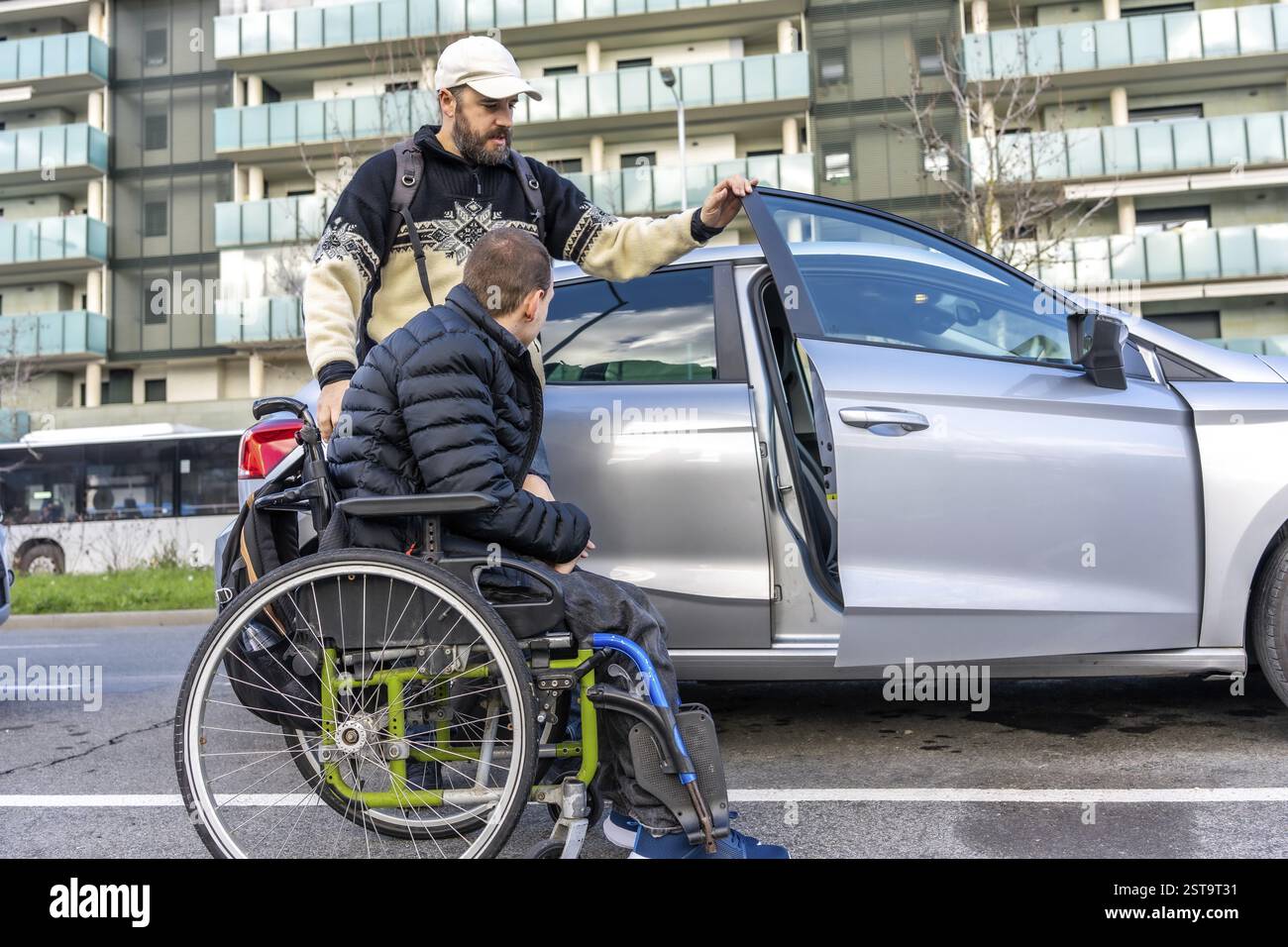 Caregiver assisting a young disabled man in a wheelchair while entering ...