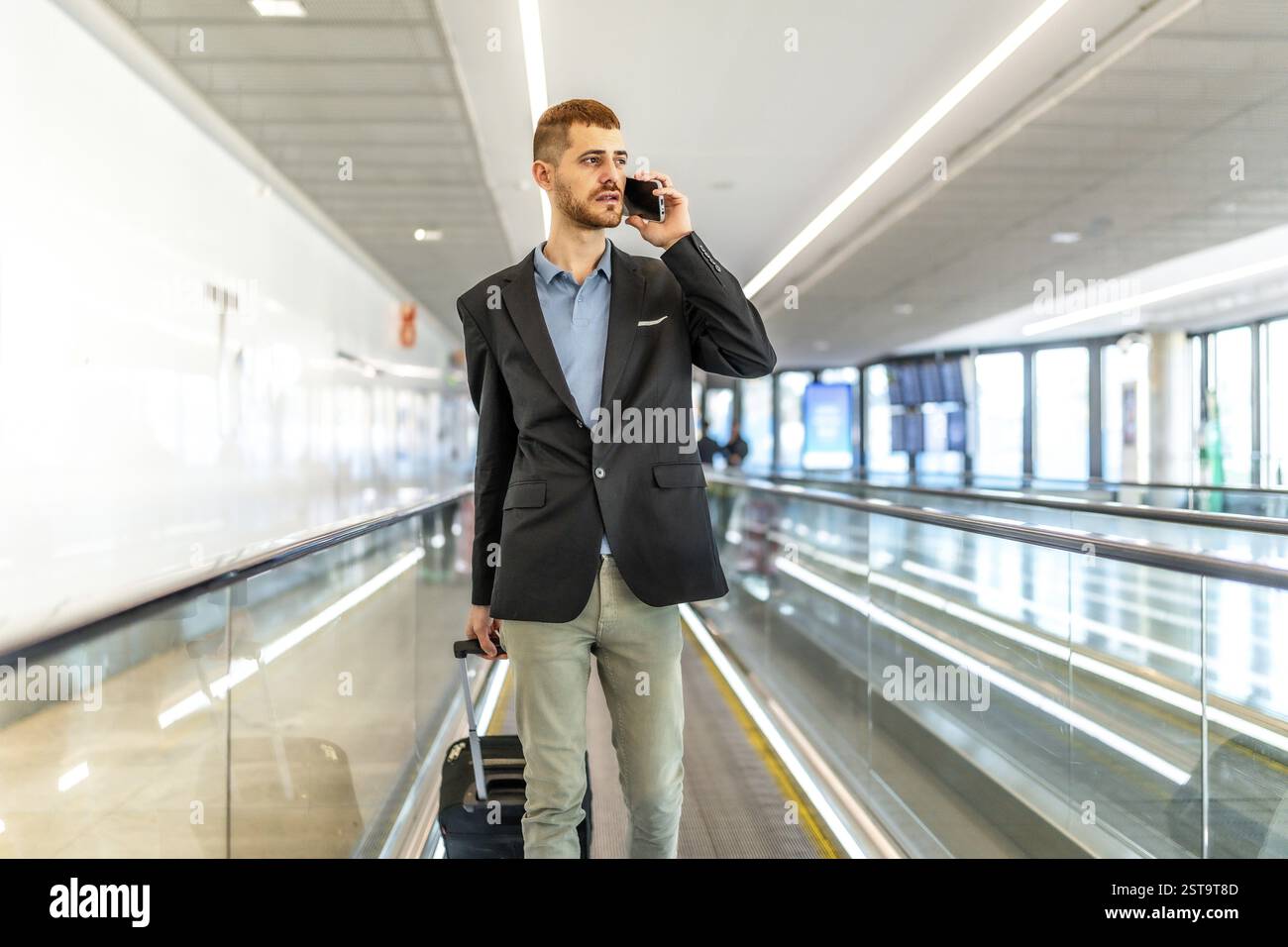 Businessman pulling suitcase and talking on smartphone while walking on ...