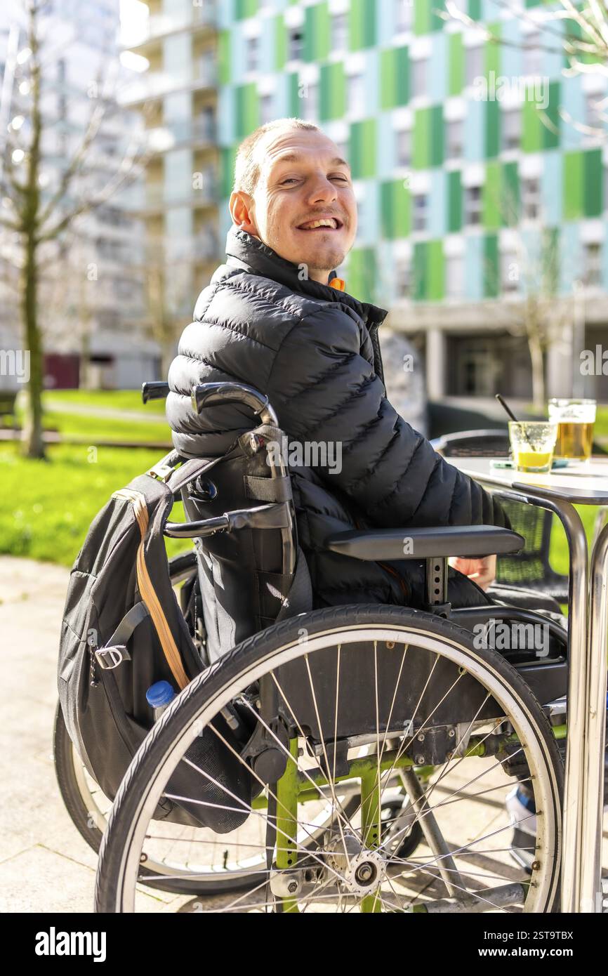 Happy disabled man sitting in a wheelchair, enjoying a refreshing drink ...