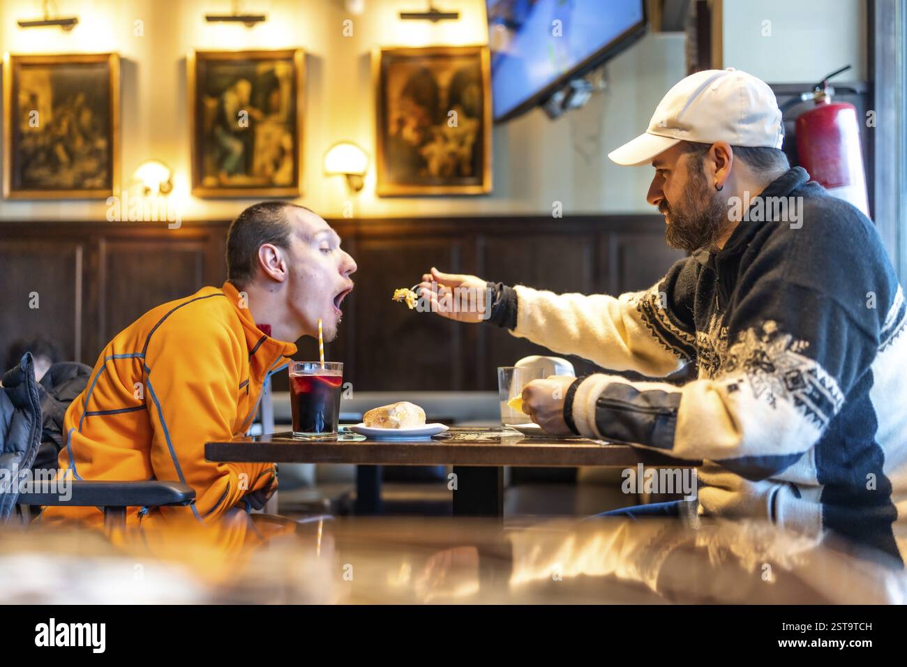 Caregiver tenderly feeds a disabled man in a restaurant, highlighting ...