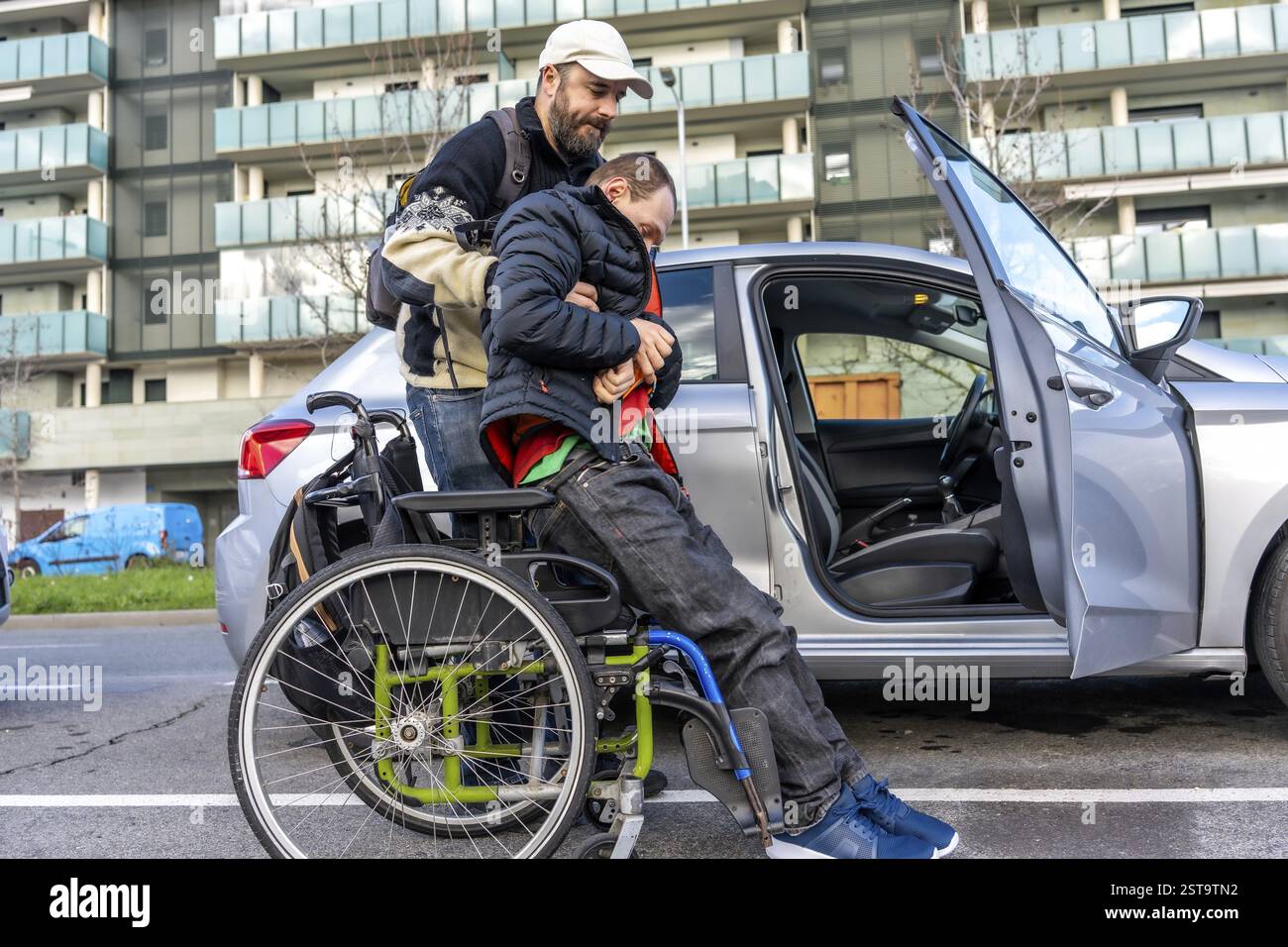 Man assisting disabled friend in getting out of a car parked on an ...