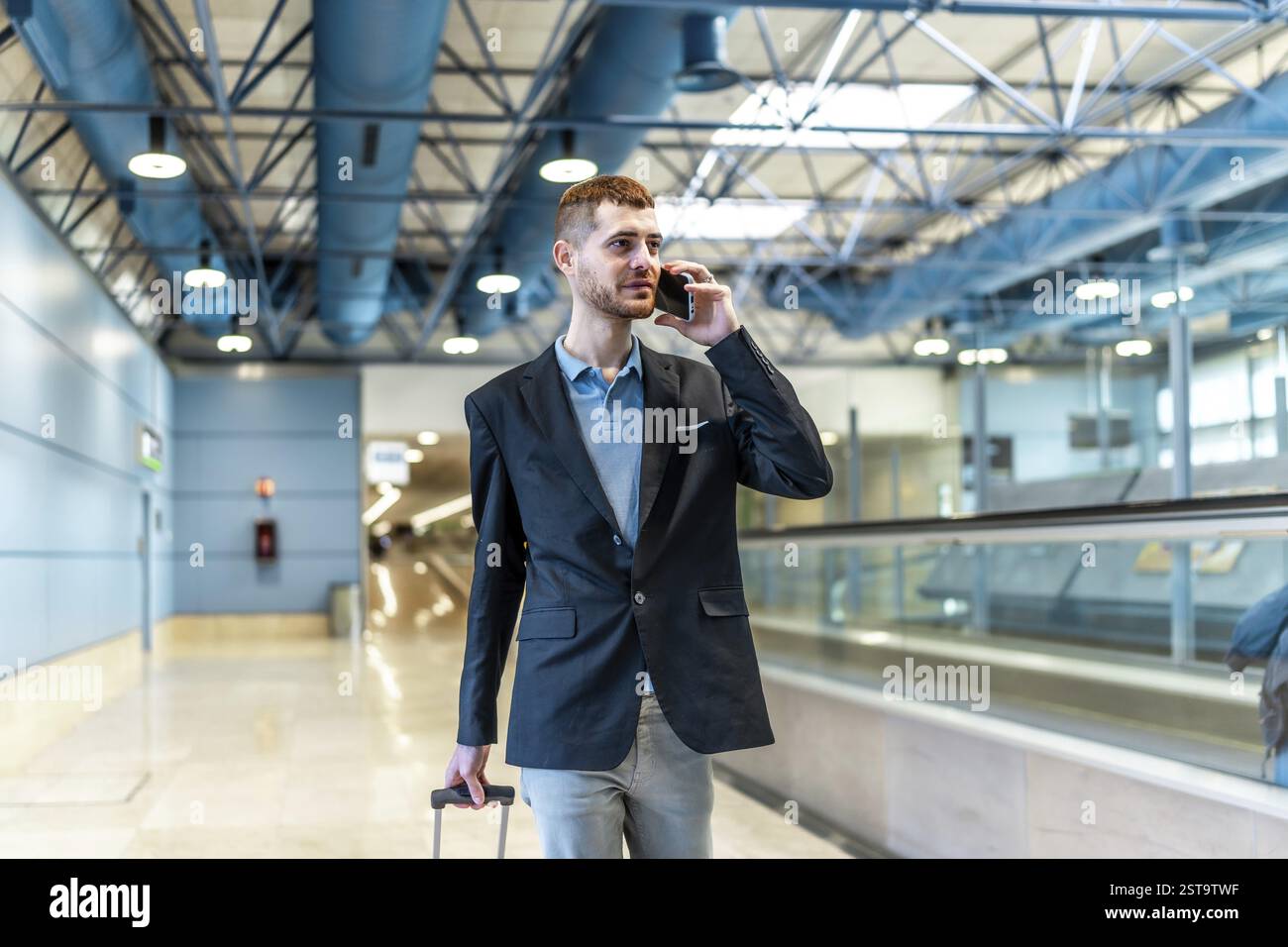 Businessman pulling suitcase and making phone call while walking ...