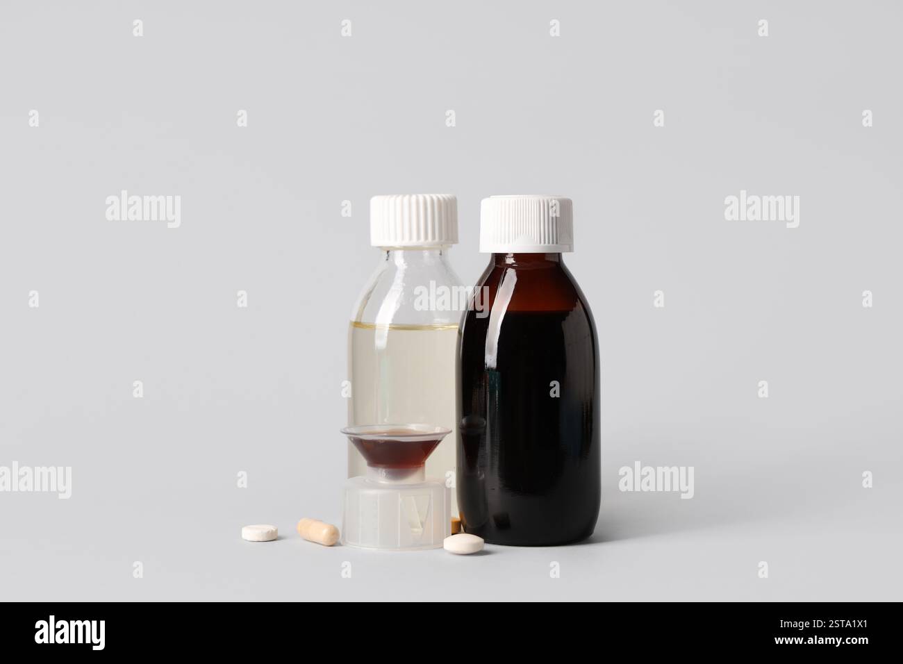 Bottles and measuring cup of cough syrup with different pills on grey ...