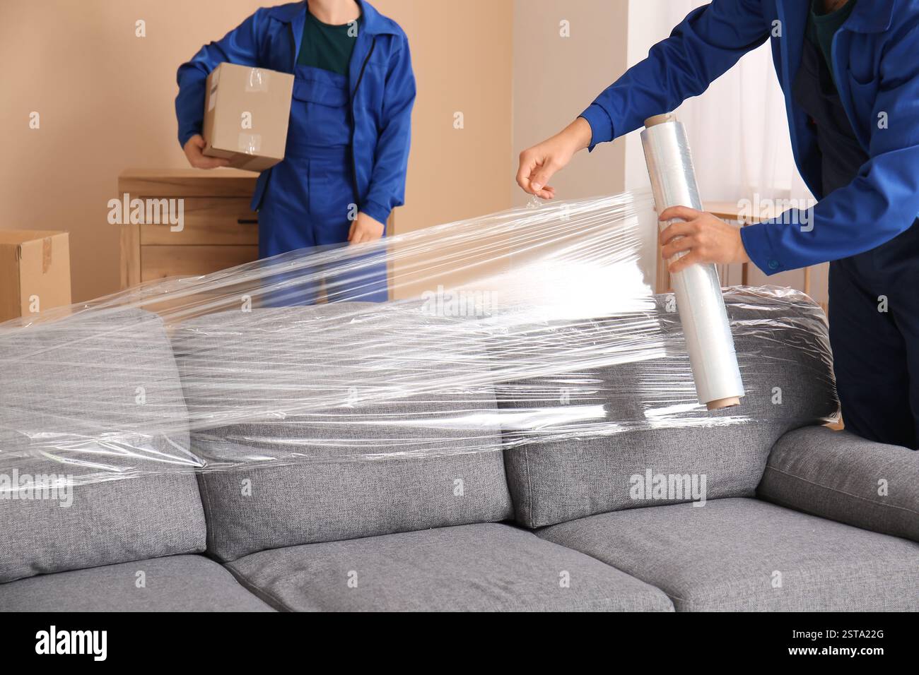 Male worker wrapping sofa with stretch film in room Stock Photo - Alamy