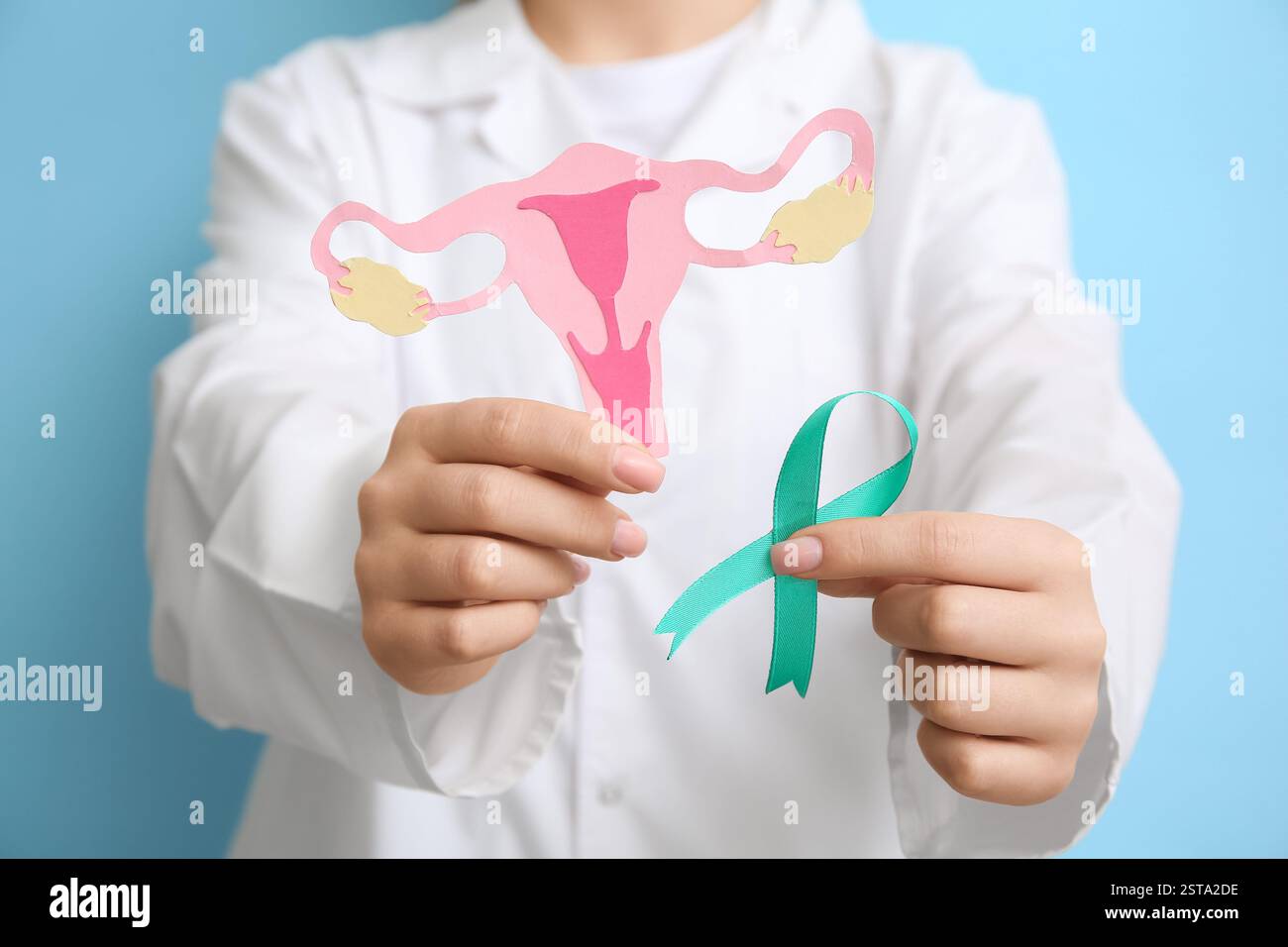 Female doctor holding turquoise ribbon with paper uterus on blue ...