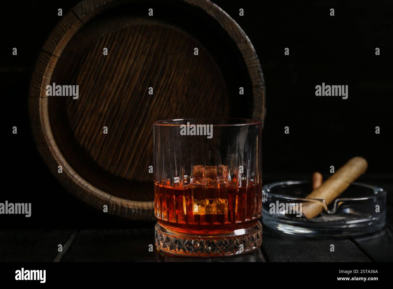 Glass of cold rum and cigar in ashtray near barrel on black wooden ...
