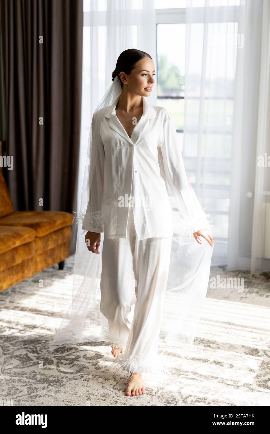 Beautiful bride wearing white pajamas and veil getting ready for ...