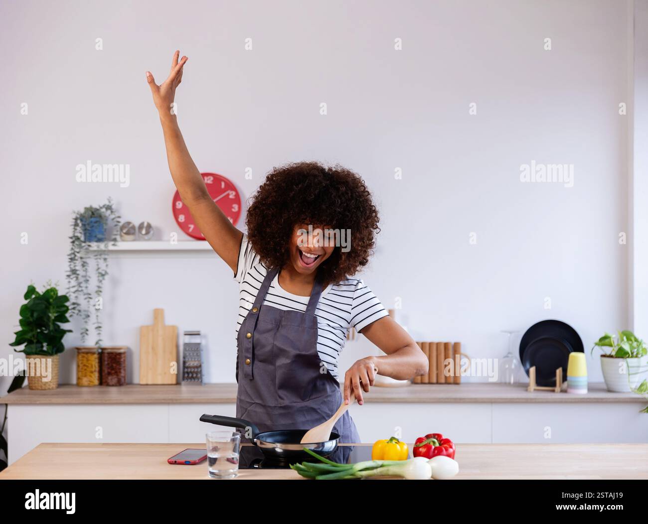 Young woman dancing while cooking fresh vegetables in modern kitchen ...