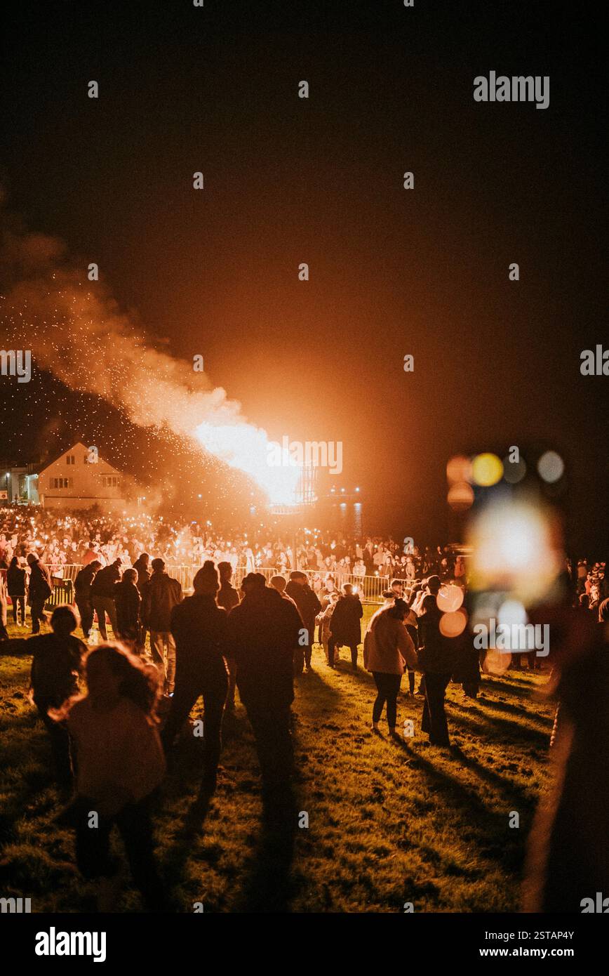 A large crowd of people are gathered around a fire, with some taking ...