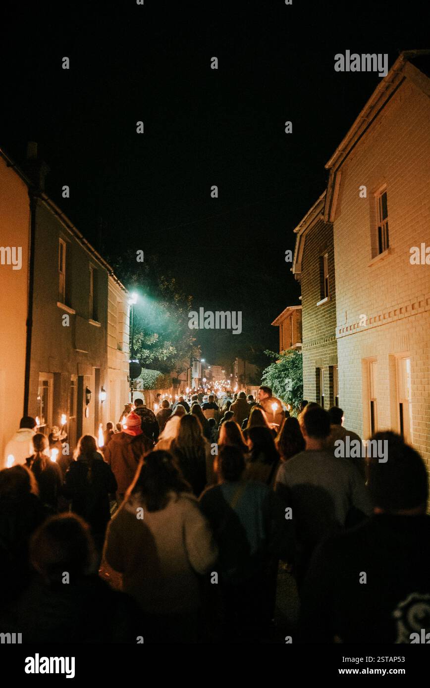 A large crowd of people are gathered in a narrow street at night. The ...