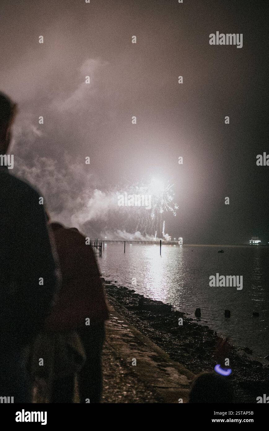 A man and woman are standing on a beach at night, watching fireworks ...
