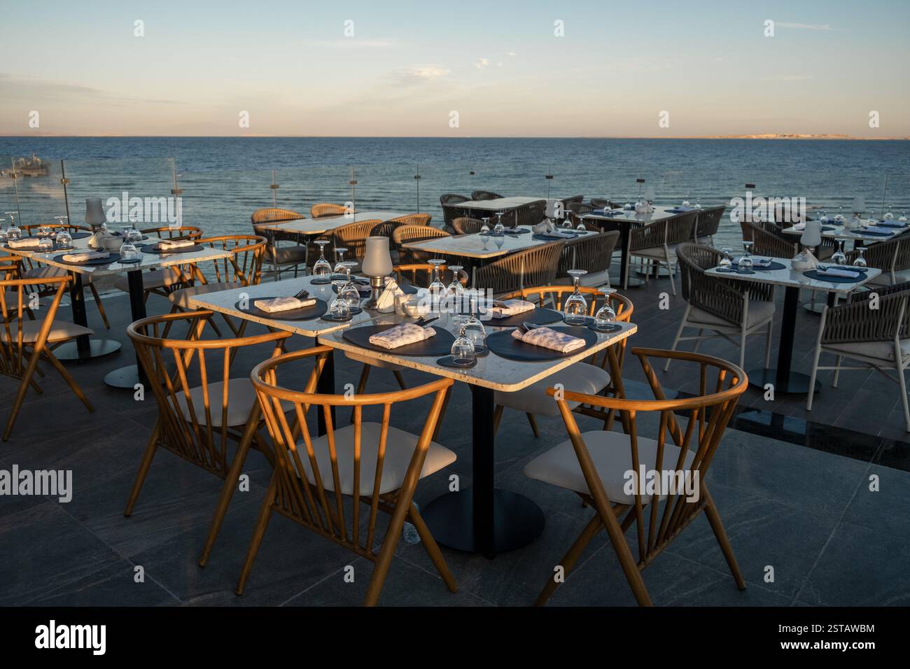 Golden sunset casts a warm glow over elegantly set tables at a seaside ...