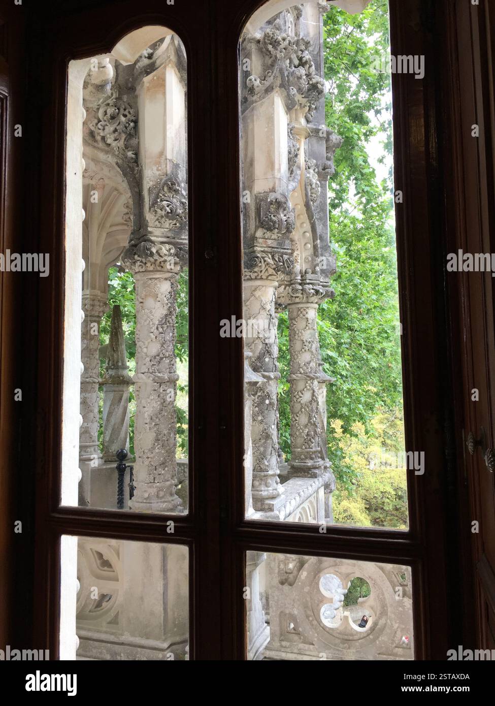 Window view with ornate stone balcony overlooking lush green garden ...