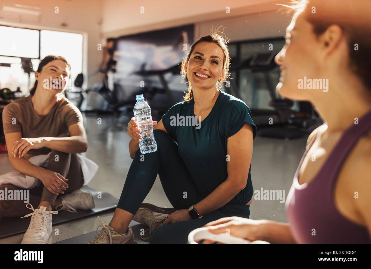 Three women siting on the gym floor, laughing and chatting after a ...