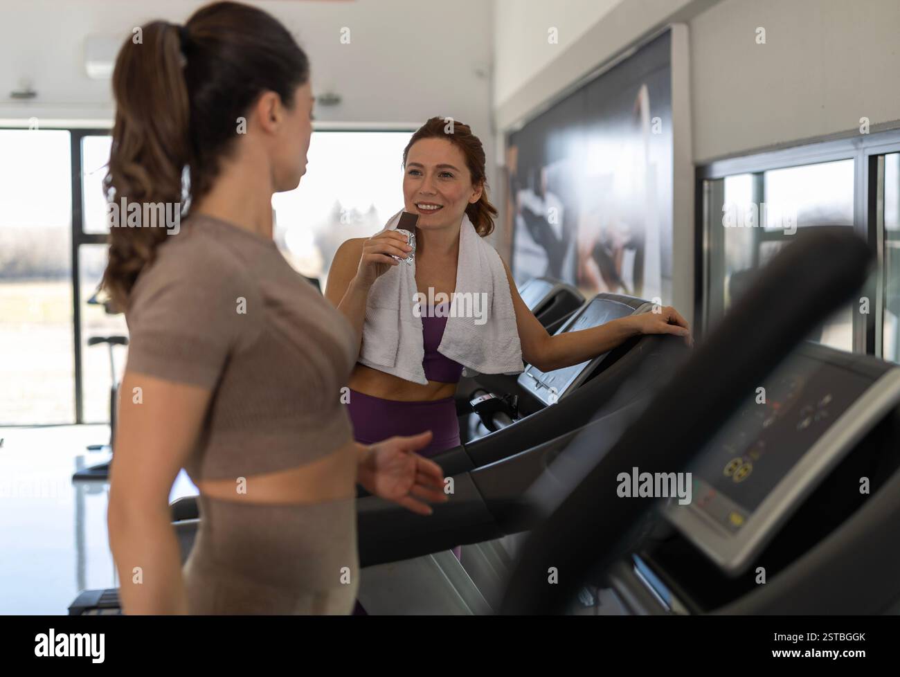 Two women engage in conversation while using treadmills, enjoying their ...